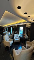 Um interior moderno com área de estar, com poltronas brancas e um espelho grande que reflete o espaço.