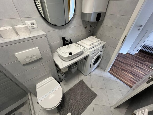 Casa de banho moderna com sanita, lavatório e máquina de lavar roupa.