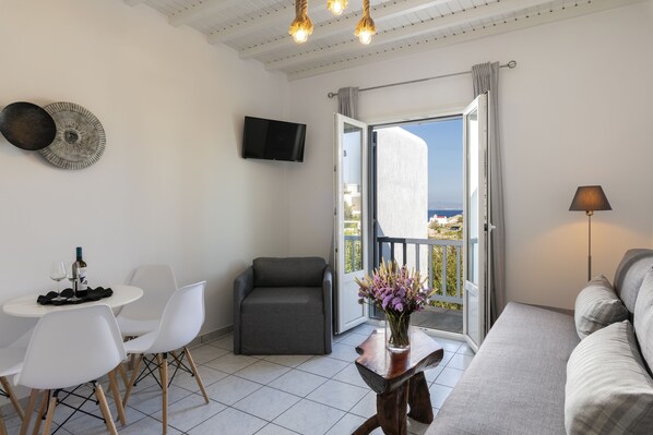 Sala de estar moderna com sofá, mesa de jantar com cadeiras, TV na parede e varanda com vista para o mar.