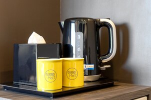 Uma cafeteira, duas canecas amarelas e uma caixa de lenços sobre uma superfície de madeira.