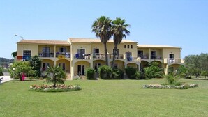 Um edifício de dois andares com fachada amarela, várias varandas e um gramado bem cuidado com palmeiras.