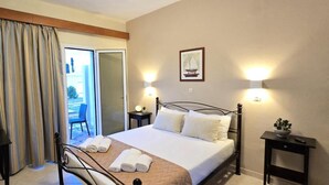 Quarto de hotel com cama, mesa de cabeceira, cadeira, pequena mesa com uma planta e vista para o exterior.