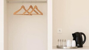Quarto minimalista com um cabideiro, chaleira e frigorífico.