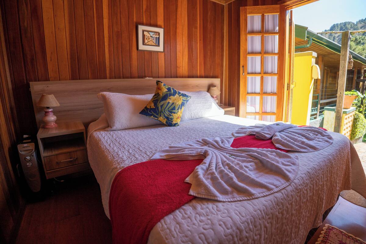 Quarto com painéis de madeira, uma cama, uma mesa de cabeceira e janela com cortinas.