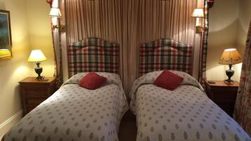 Quarto duplo com duas camas, cada uma com travesseiro vermelho, e mesas de cabeceira laterais com abajures.