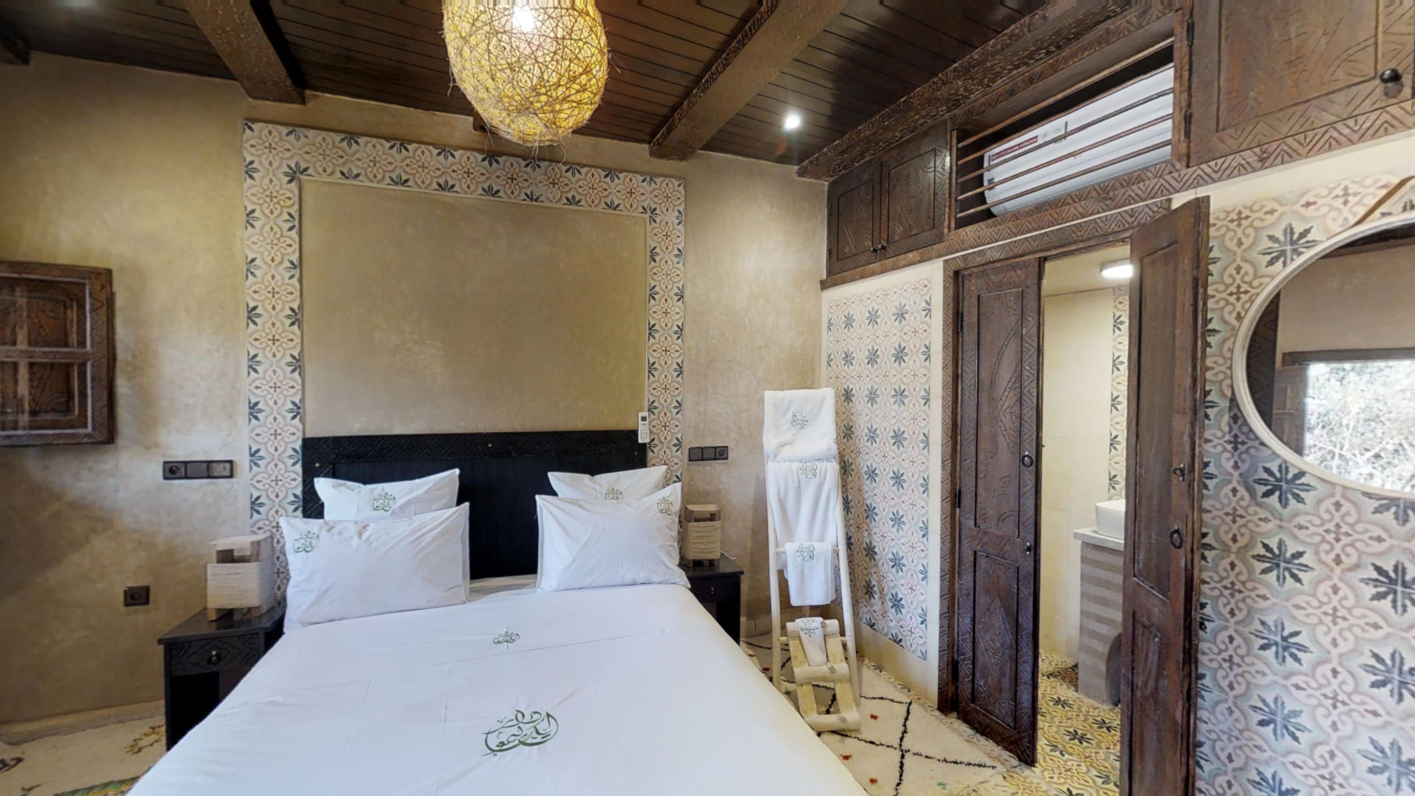 Quarto com cama grande, teto de madeira, paredes estampadas e espelho.