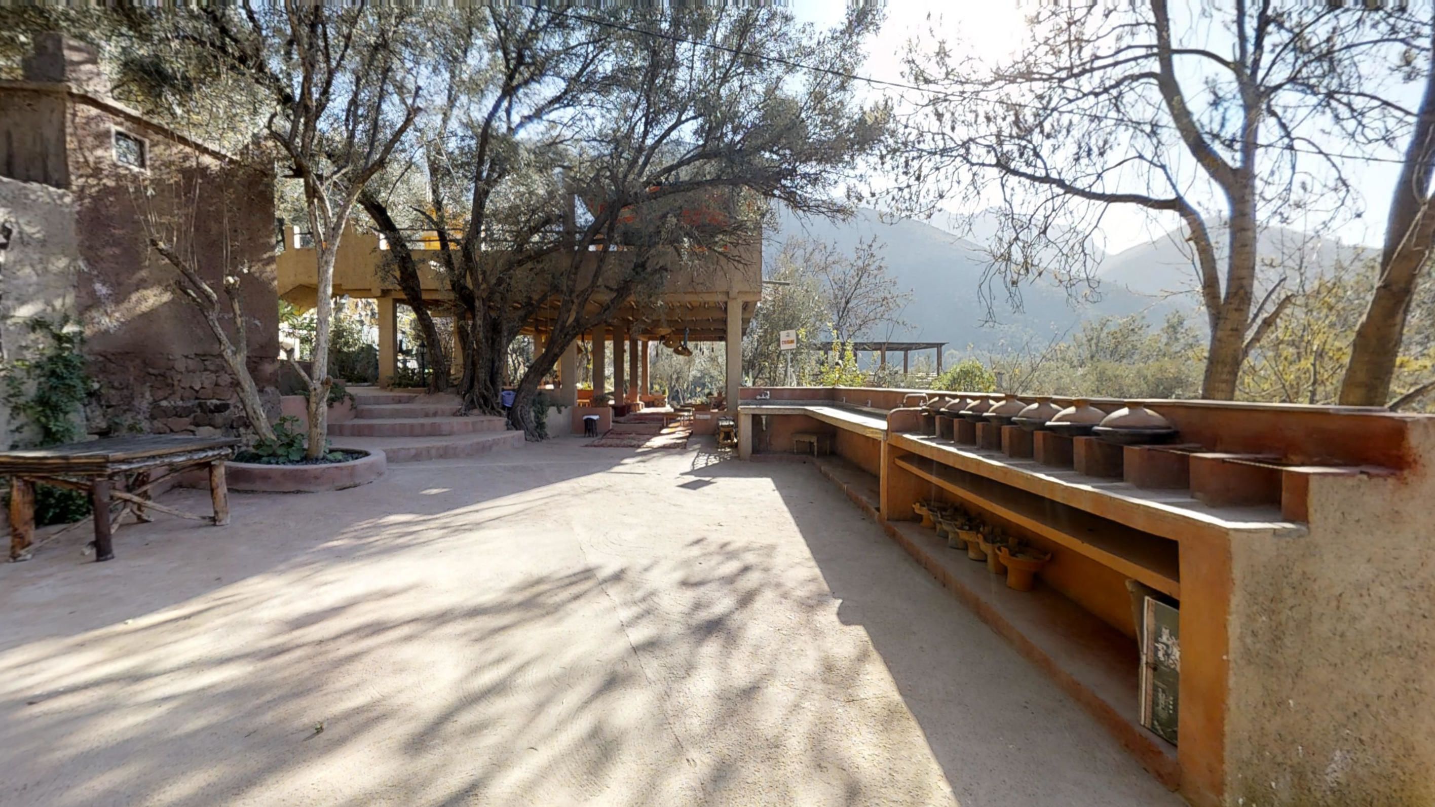 Área de terraço ao ar livre com pérgola, assentos e um balcão comprido com vasos.