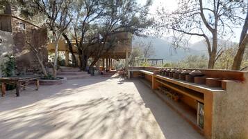 Área de terraço ao ar livre com pérgola, assentos e um balcão comprido com vasos.