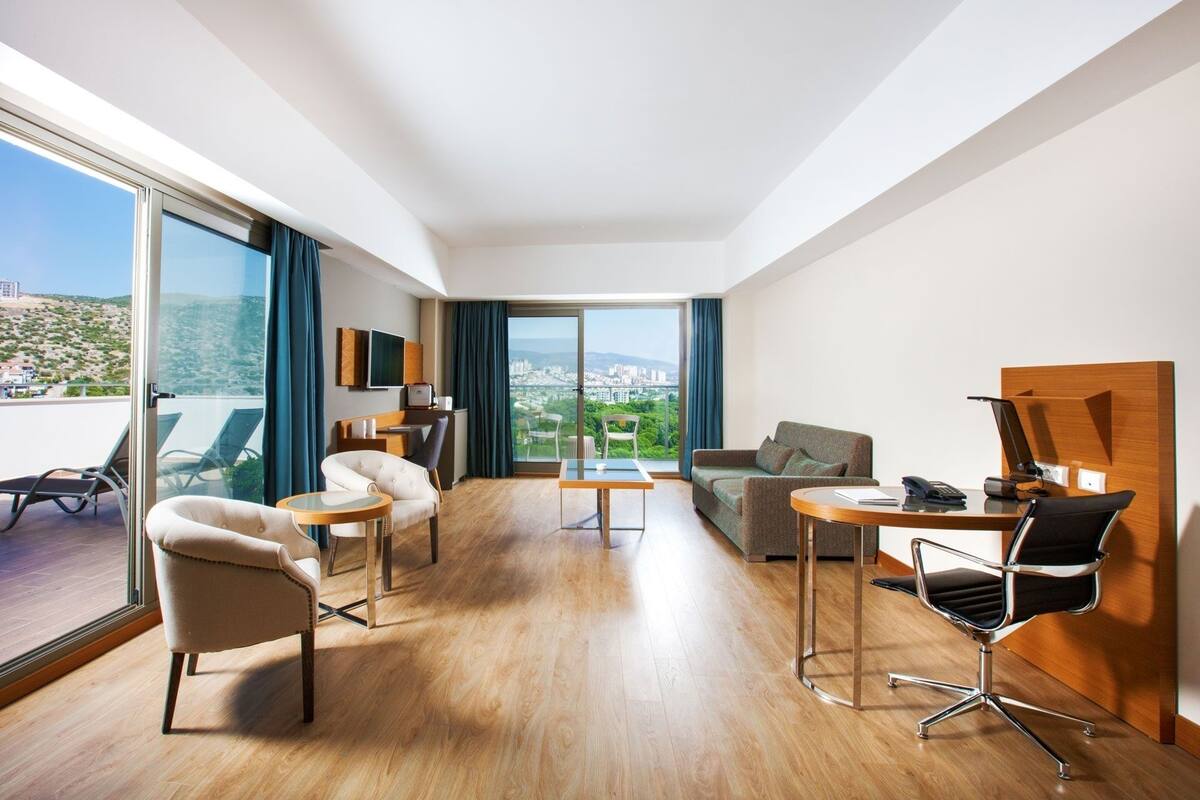 Quarto de hotel moderno com varanda, sofá, escrivaninha e cadeira.