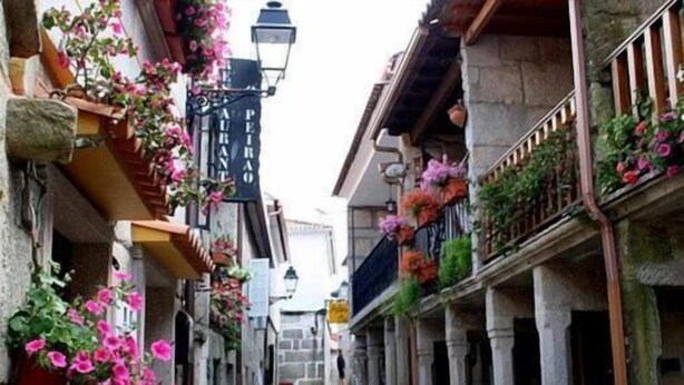 Uma rua estreita ladeada por edifícios, alguns com varandas decoradas com flores.