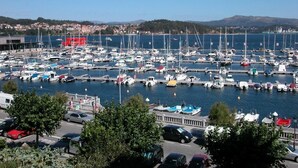 Marina com vários barcos atracados, céu claro e uma cidade ao longe.