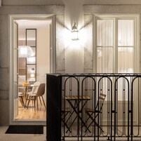 Um interior moderno com uma porta de vidro que dá para uma área de refeições, uma cerca de metal preto e uma parede texturizada com um ponto de luz fixado na parede.