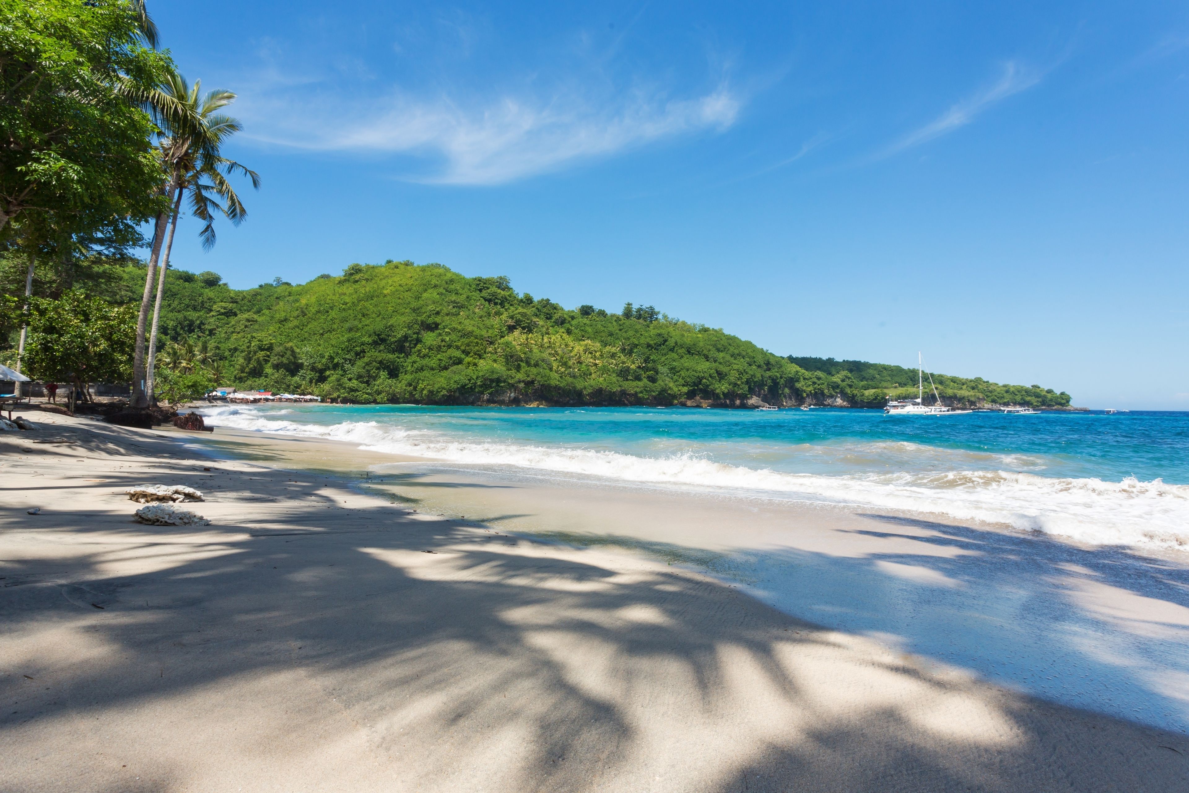 Uma praia com águas turquesa cristalinas, areia branca e colinas verdes exuberantes ao fundo.