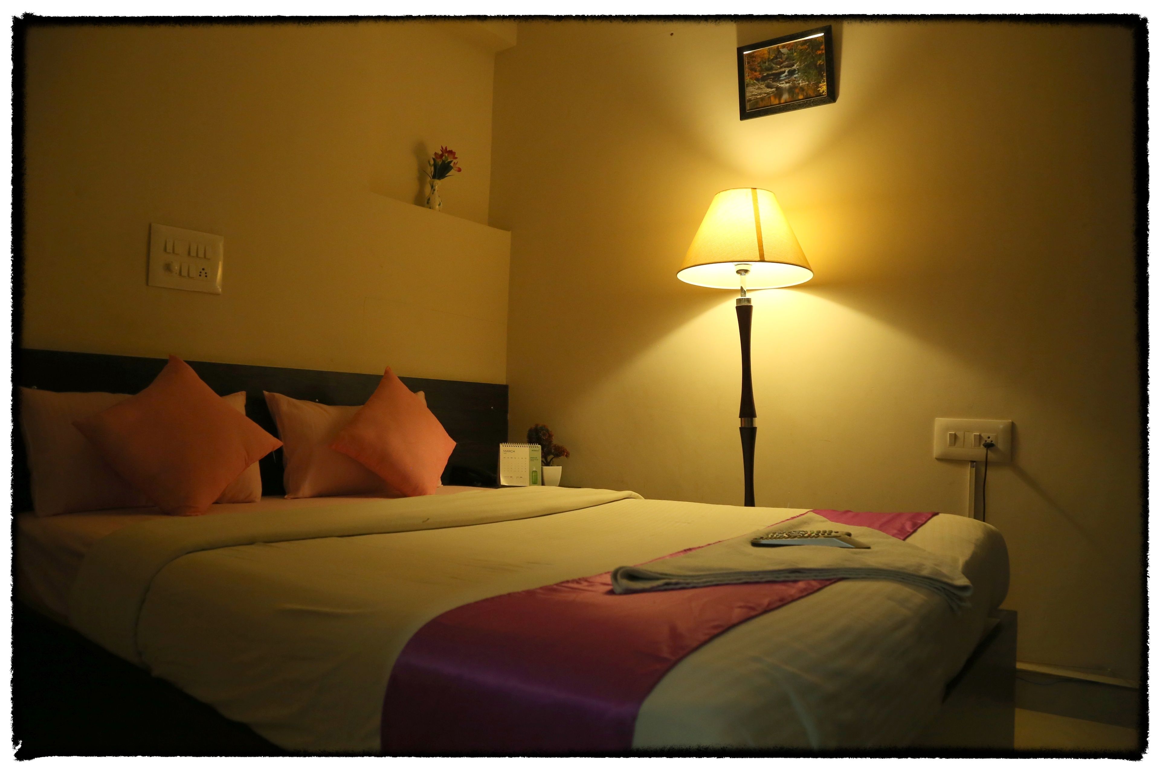 Quarto de hotel com duas camas, uma mesa de cabeceira, um abajur e uma tomada na parede.