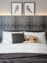 Uma cama com roupa de cama branca, duas almofadas estampadas e uma cabeceira cinza com um desenho decorativo.