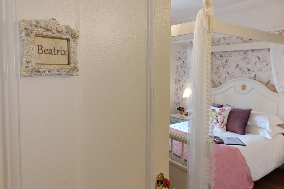 Quarto com cama de dossel, mesa de cabeceira com luminária e papel de parede floral.