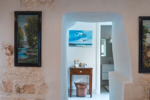 Um corredor com paredes de pedra rústica, uma mesa de madeira com um balde e obras de arte emolduradas.