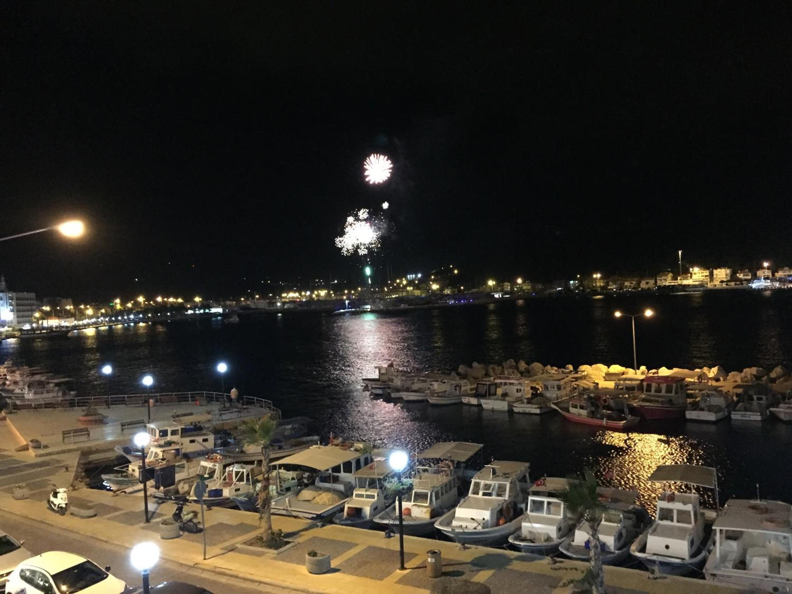Marina à noite com barcos atracados, postes de luz e paisagem urbana ao fundo.