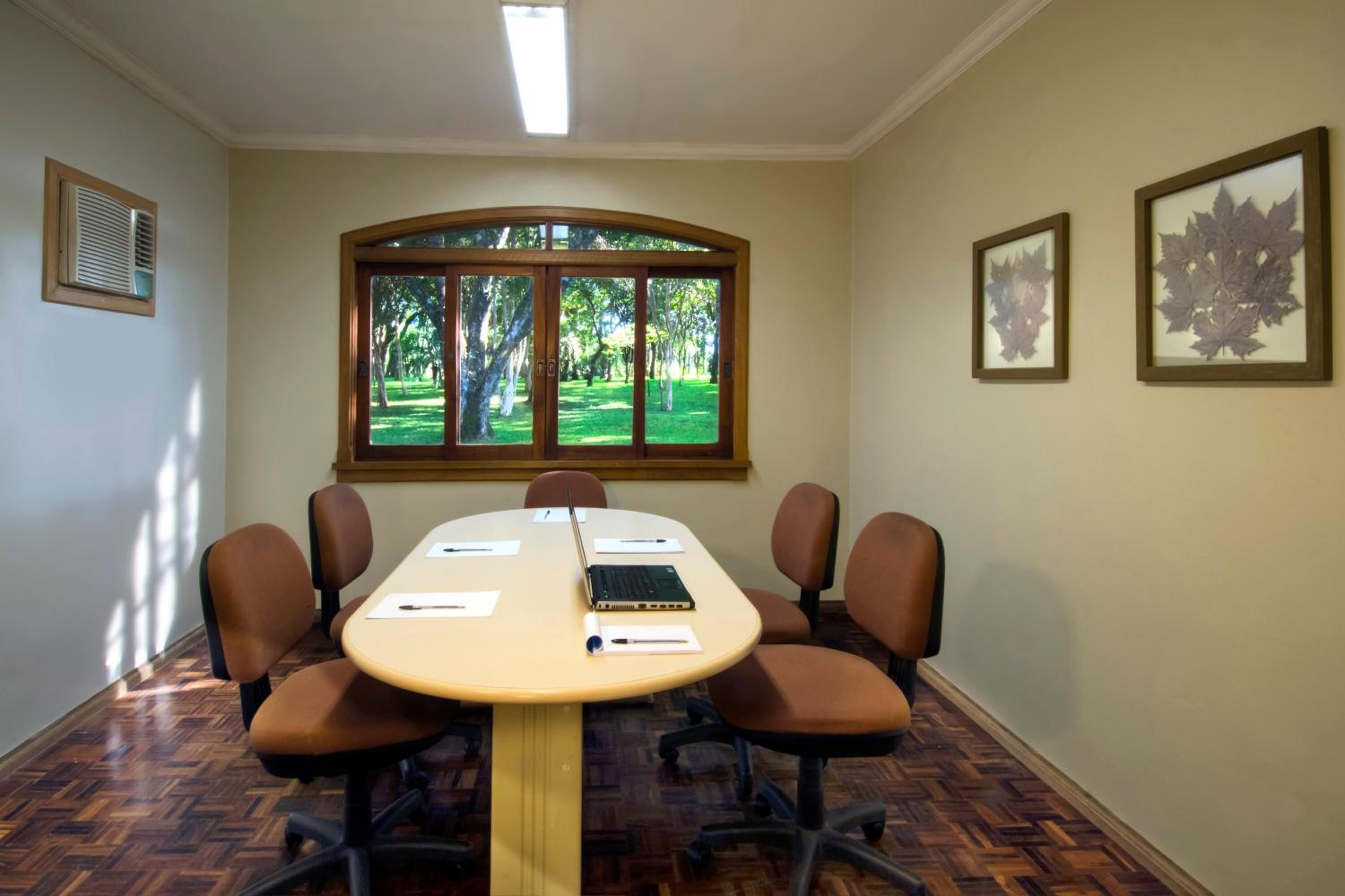 Uma sala de conferências com uma mesa grande, seis cadeiras, um laptop e quadros nas paredes.