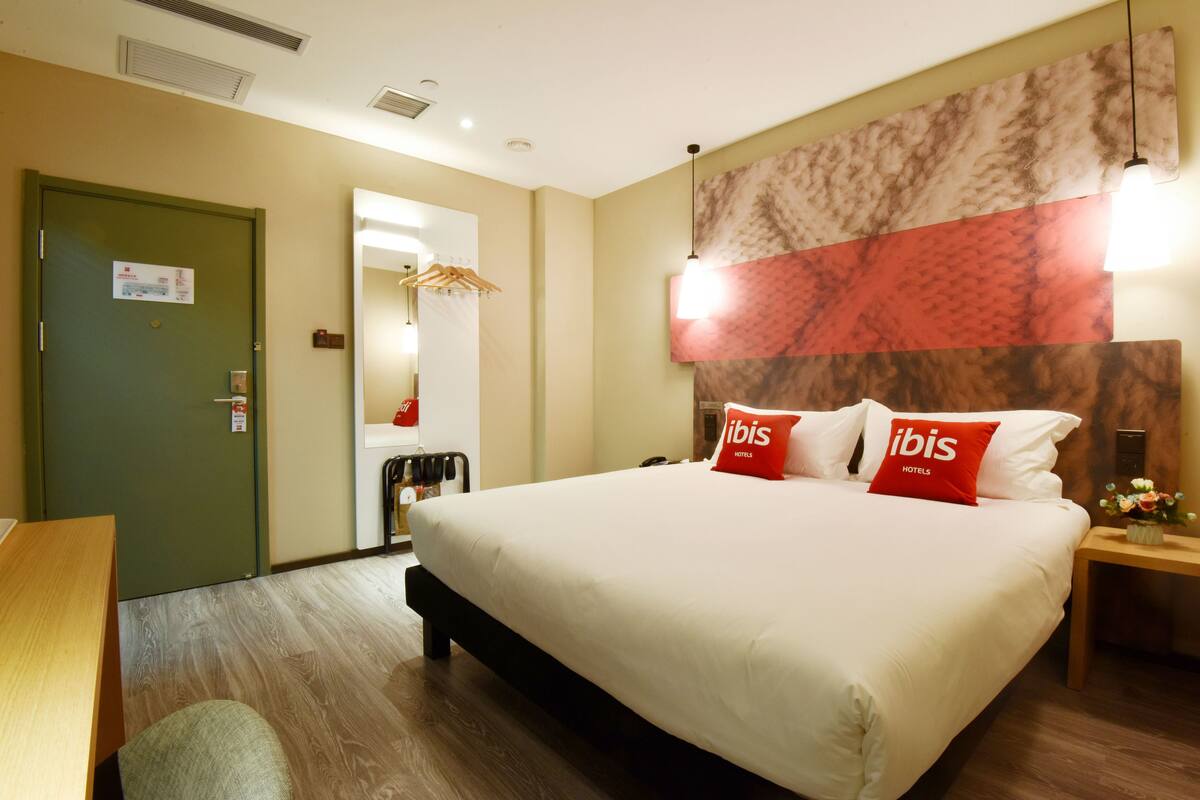 Quarto de hotel com uma cama grande, uma escrivaninha e um guarda-roupa.