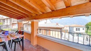 Área externa coberta com mesa posta para refeições, vista do bairro circundante e estrutura de teto em madeira.