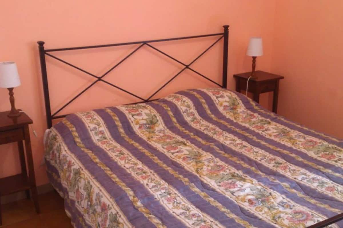 Quarto com cama, cabeceira, duas mesas de cabeceira e luminárias.