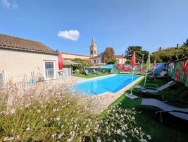 Piscina com espreguiçadeiras e guarda-sóis, cercada por um jardim com flores e um mural.