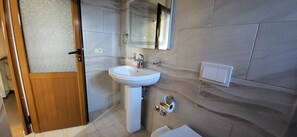 Casa de banho com lavatório branco, espelho e área de duche.