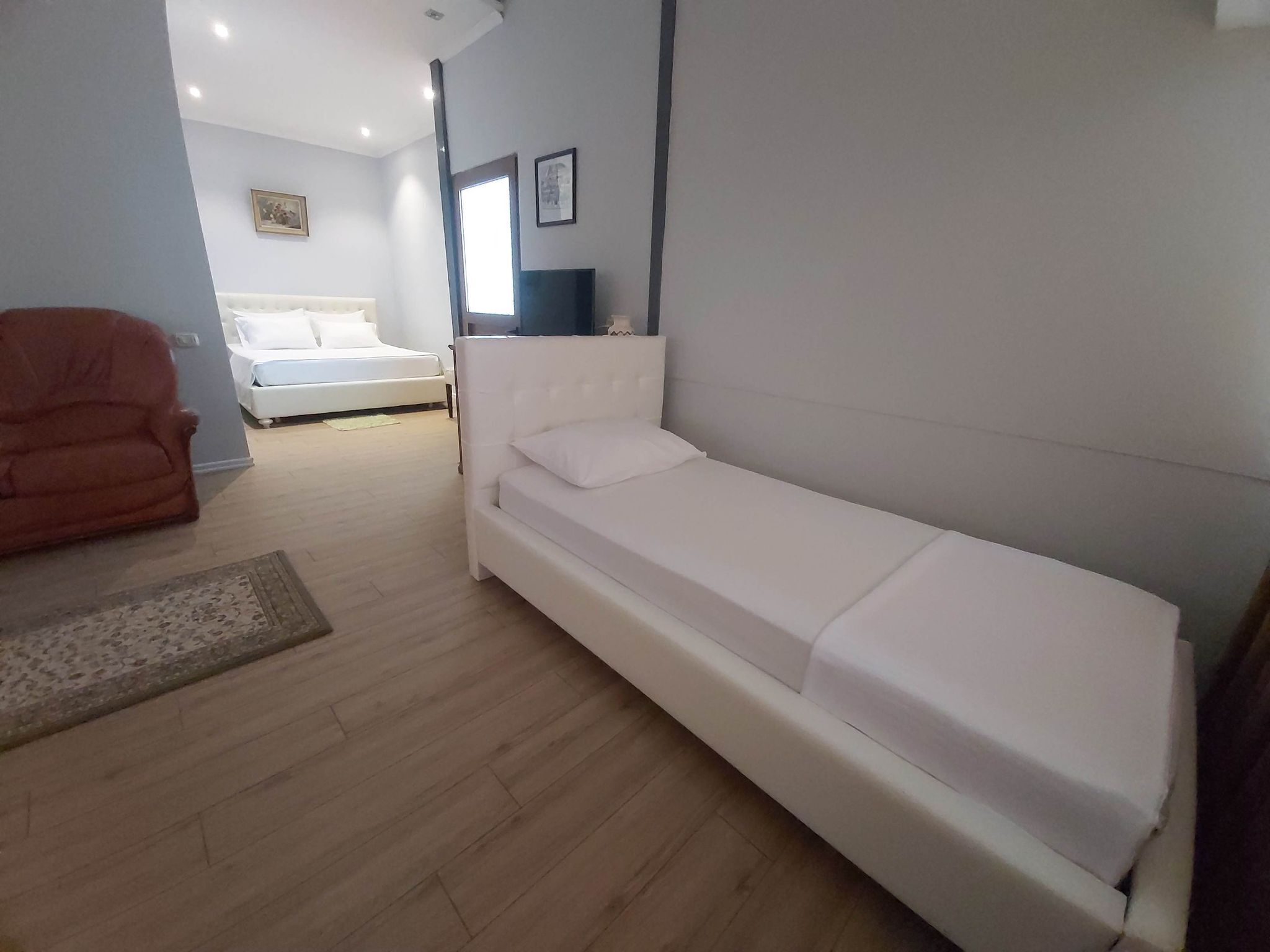 Quarto moderno e minimalista com uma cama de casal branca, uma poltrona vermelha e uma mesinha.