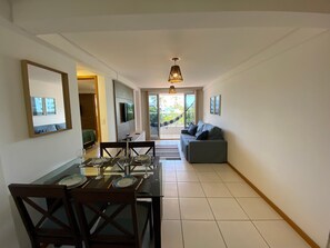 Uma sala de jantar com uma mesa posta para quatro pessoas, um sofá, uma televisão presa na parede e vista para o exterior.