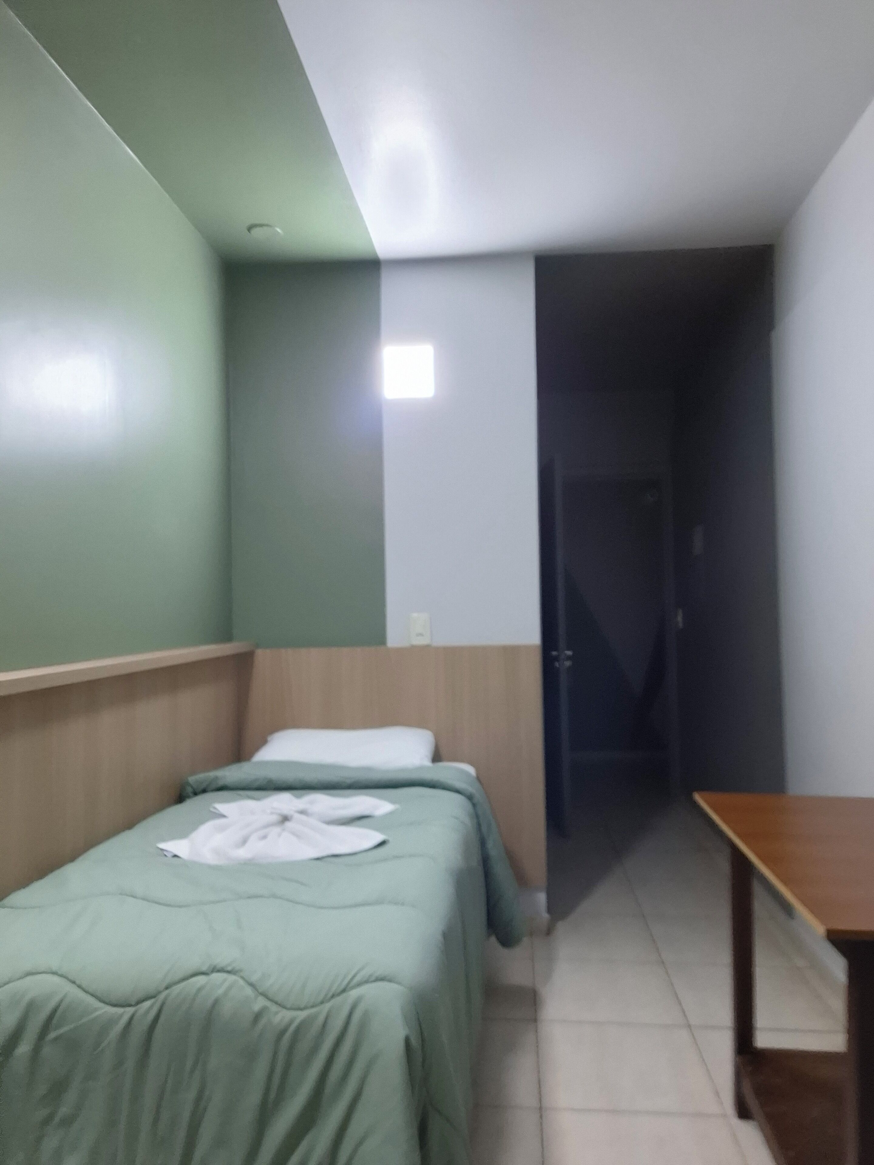 Um quarto com uma cama, uma mesa de madeira e uma porta que dá para outro cômodo.