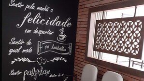 Quarto com parede preta exibindo frases motivacionais em português, uma janela com tela decorativa e duas cadeiras brancas.