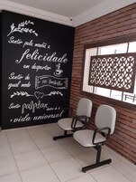 Quarto com parede preta exibindo frases motivacionais em português, uma janela com tela decorativa e duas cadeiras brancas.