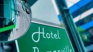 Uma placa verde com o texto 'Hotel Romanville' em frente a um edifício moderno.