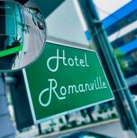 Uma placa verde com o texto 'Hotel Romanville' em frente a um edifício moderno.