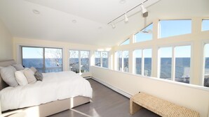 Quarto com uma cama grande, várias janelas e vista para o mar.