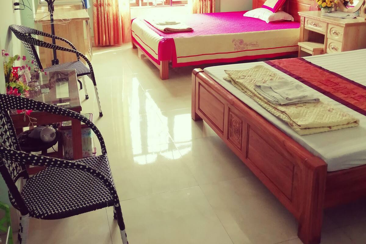 Quarto de hotel com duas camas, área de refeições com mesa e cadeiras, um espelho e uma janela com cortinas.