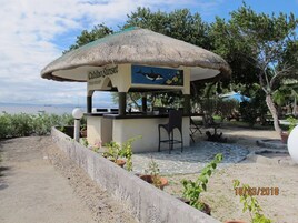 Um quiosque à beira-mar chamado 'Cabiltao Sunset Beach Resort', com telhado de palha, área de estar e plantas em vasos.