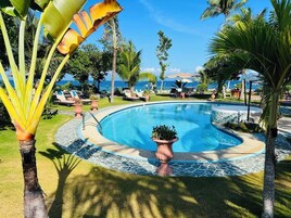 Área da piscina com espreguiçadeiras, palmeiras e vista para o mar.