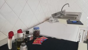 Cozinha com painel de azulejos branco, pia de aço inoxidável e diversos utensílios sobre o balcão.