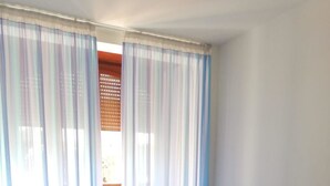Quarto de hotel com cama, uma cadeira e janela com cortinas.
