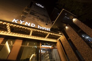 Exterior do hotel KYND com luzes de letreiro iluminadas e uma grande placa.