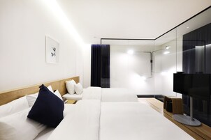 Quarto de hotel moderno com uma cama grande, uma mesa de cabeceira, televisão e área de chuveiro.