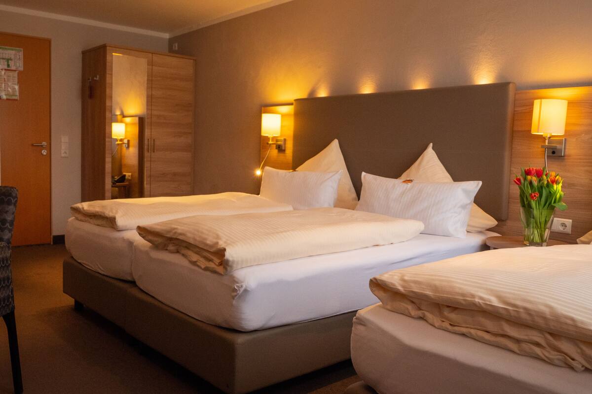 Quarto de hotel com duas camas, uma cadeira e um vaso de flores.