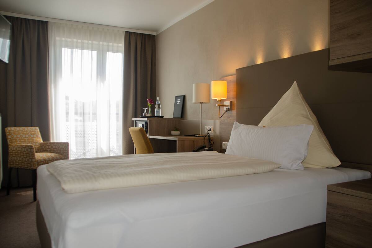Quarto de hotel com uma cama grande, uma escrivaninha, uma cadeira e uma luminária.