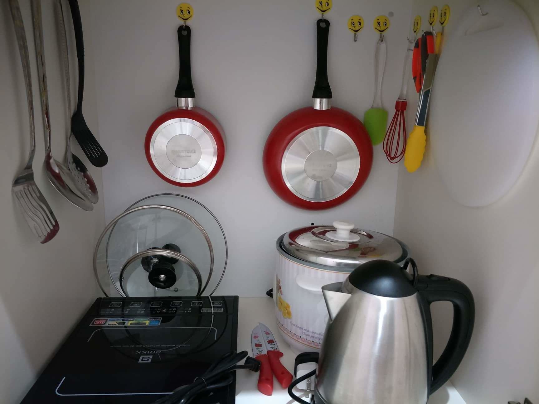 Uma cozinha com um cozedor de arroz, uma chaleira e vários utensílios pendurados na parede.