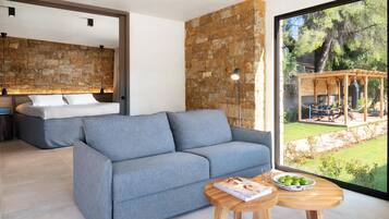 Sala de estar moderna com sofá cinza, mesa de centro de madeira e uma janela grande com vista para um jardim e área de estar externa.