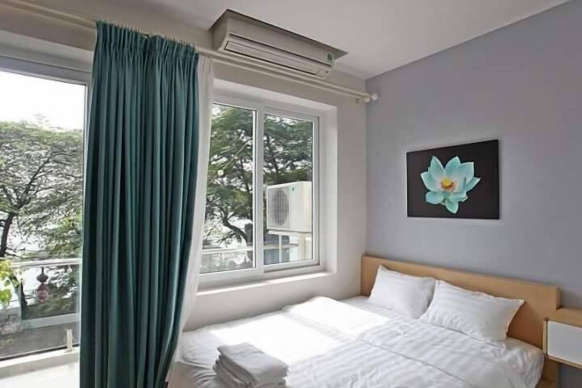 Quarto de hotel com cama, janela com cortinas, ar condicionado e pintura de flores na parede.