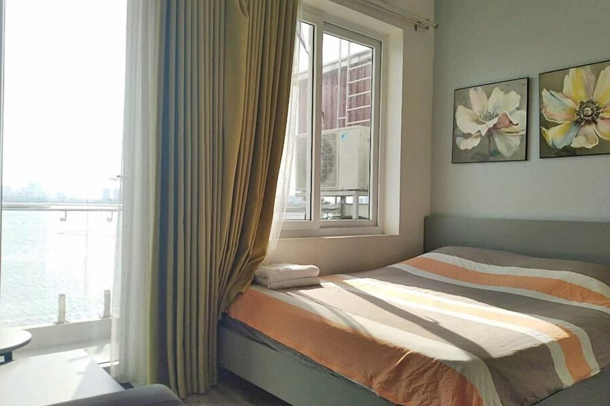 Quarto de hotel com uma cama, uma janela com cortinas e duas pinturas de flores na parede.