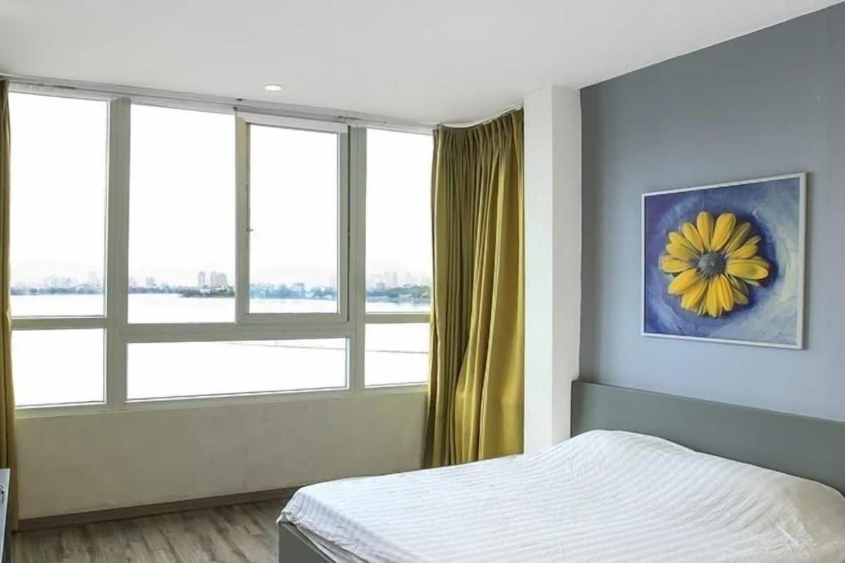 Quarto de hotel com uma janela grande, uma cama e um quadro de uma flor amarela na parede.